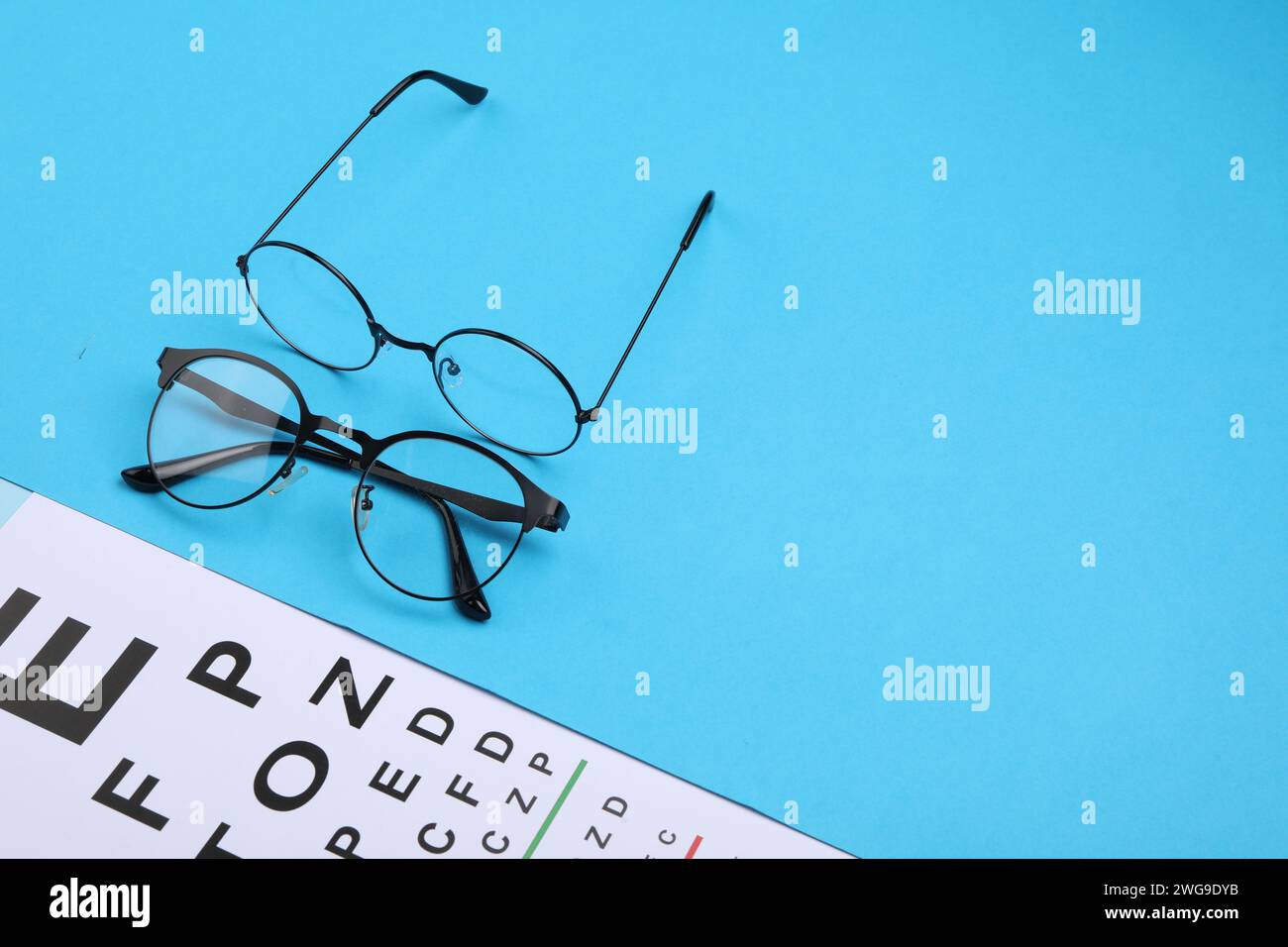 Vision test chart and glasses on light blue background, space for text ...