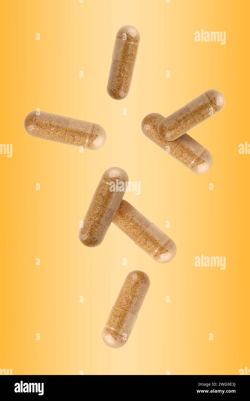 Vitamin. Capsules falling on orange gradient background Stock Photo - Alamy