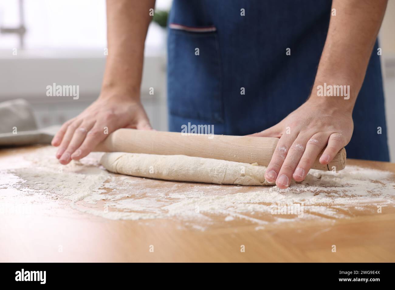 Making bread. Man rolling dough at wooden table in kitchen, closeup ...