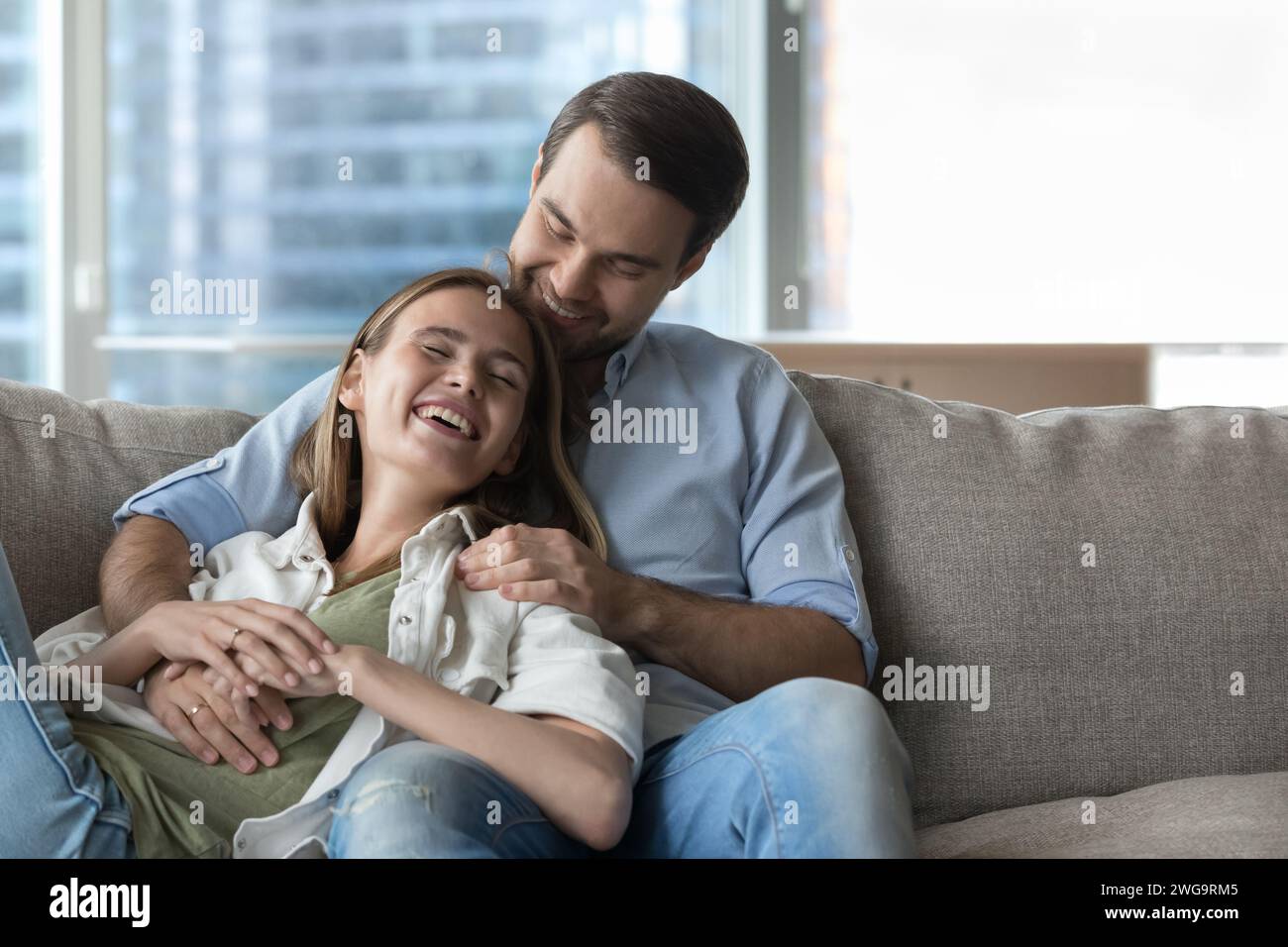 Cheerful millennial boyfriend hugs girlfriend relaxing together on sofa Stock Photo - Alamy