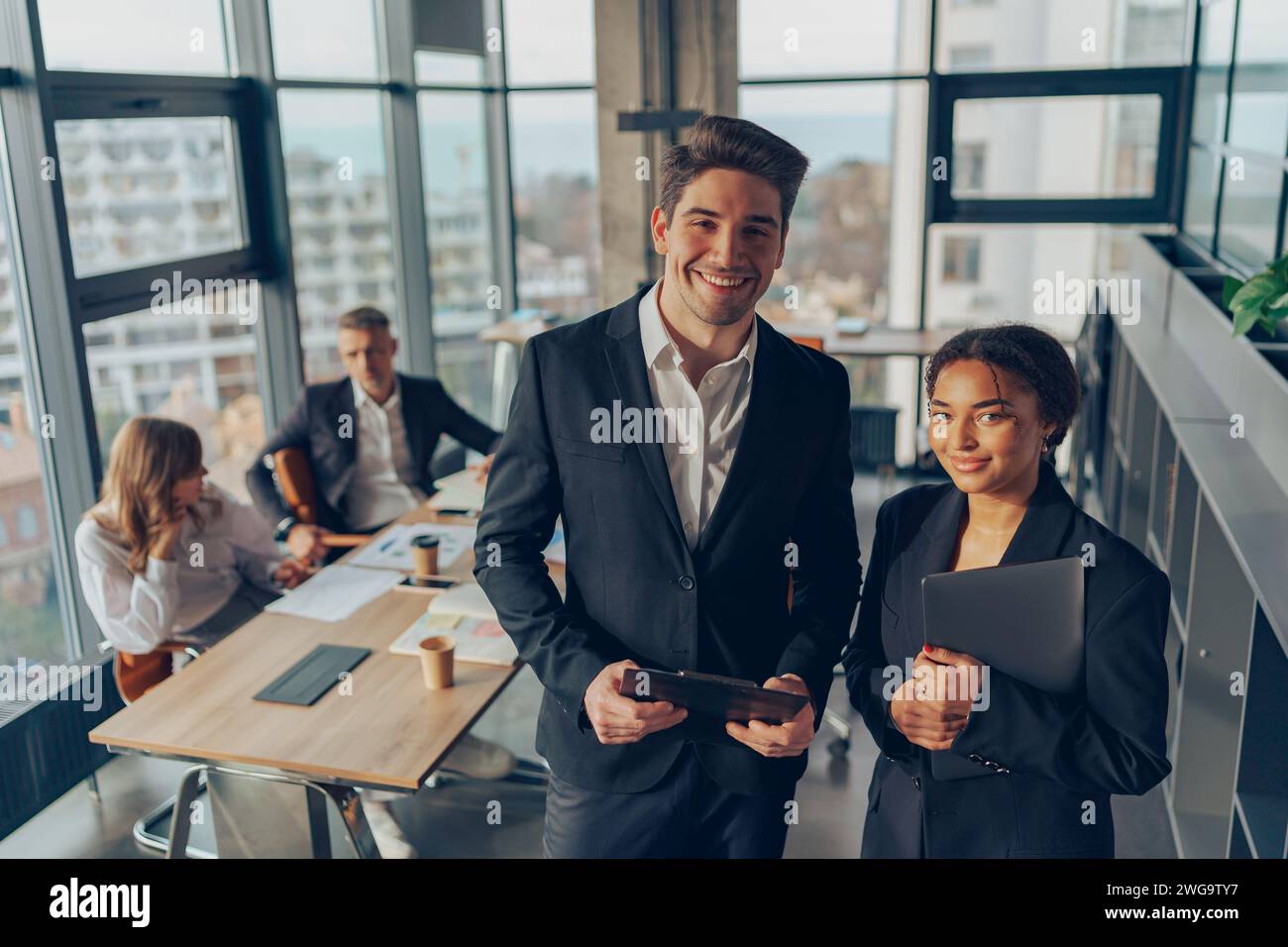 Two smiling managers standing with clipboard in office on colleagues ...