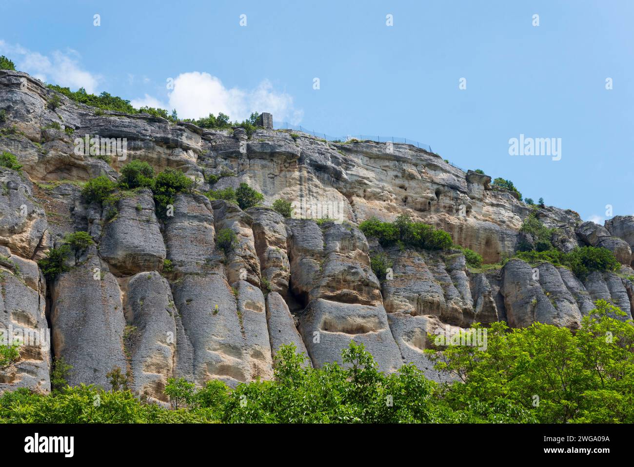 Rocky cliffs against a clear blue sky, surrounded by green vegetation ...