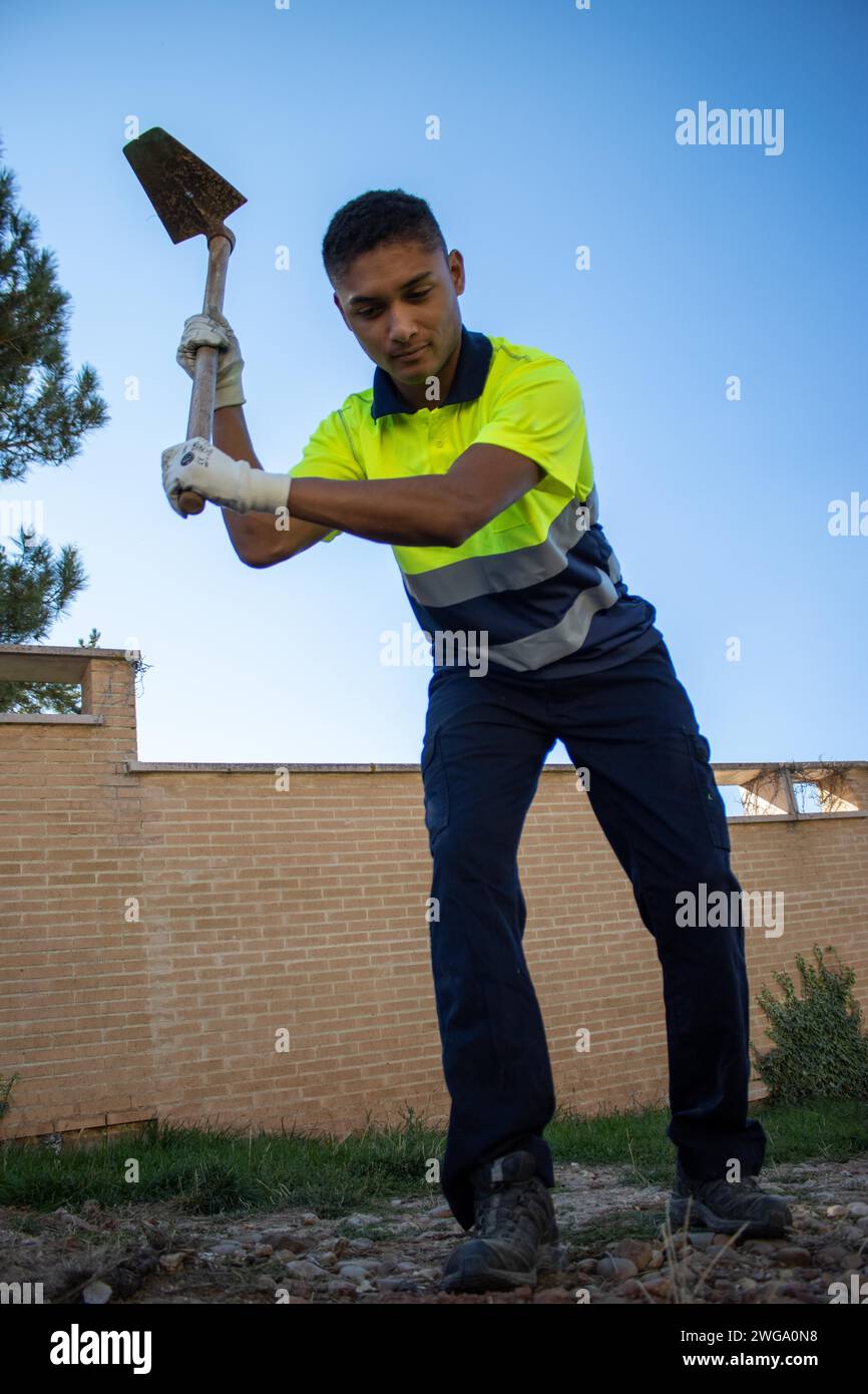 Smiling adult man in work clothes ploughing the land with a hoe ...