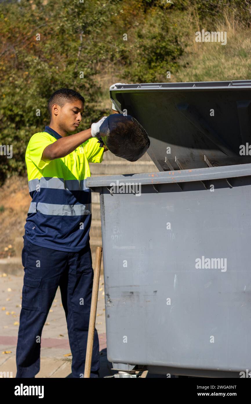 Vertical portrait of latin garbage man throwing garbage into dumpster ...