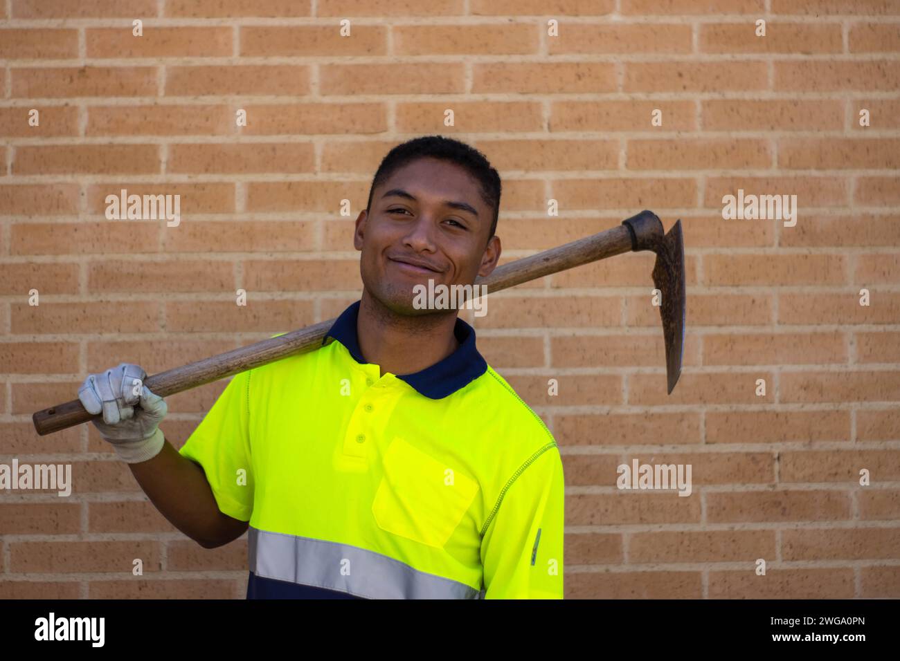 Portrait of a smiling laborer with a hoe over his shoulder looking at ...