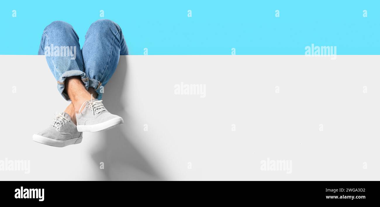 Legs of young man in jeans and blank poster on light blue background ...