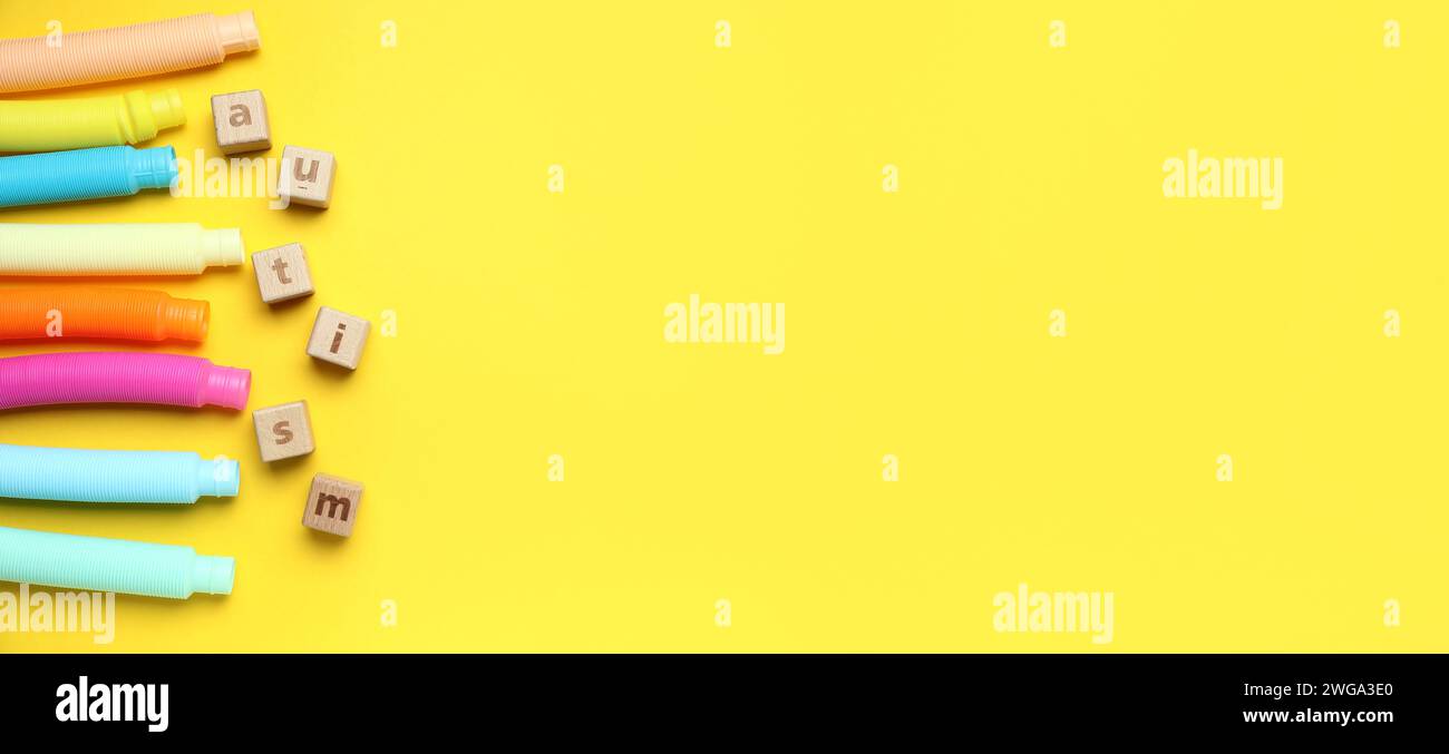 Word AUTISM made of wooden cubes and pop tubes on yellow background ...