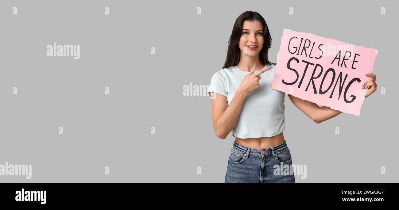 Young woman holding poster with text GIRLS ARE STRONG on grey ...