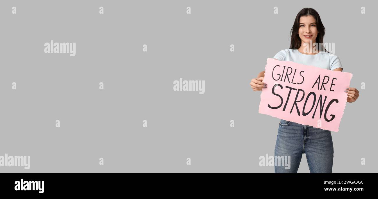 Young woman holding poster with text GIRLS ARE STRONG on grey ...