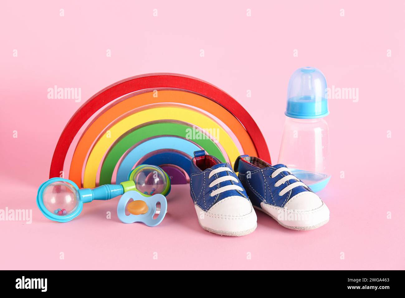 Stylish baby shoes with pacifier, rattle and bottle of milk on pink ...