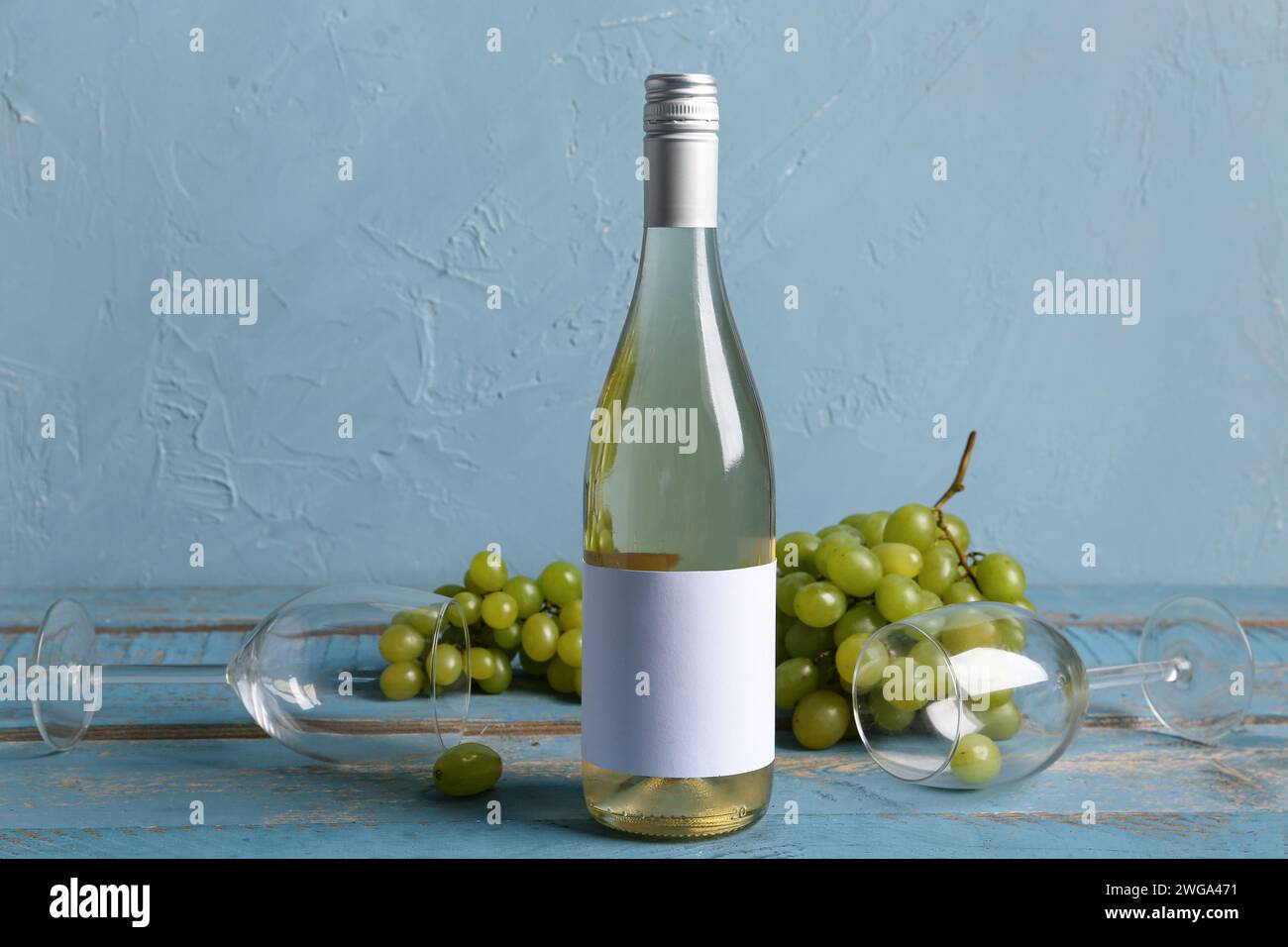 Glasses and bottle of exquisite wine with grapes on table near blue ...