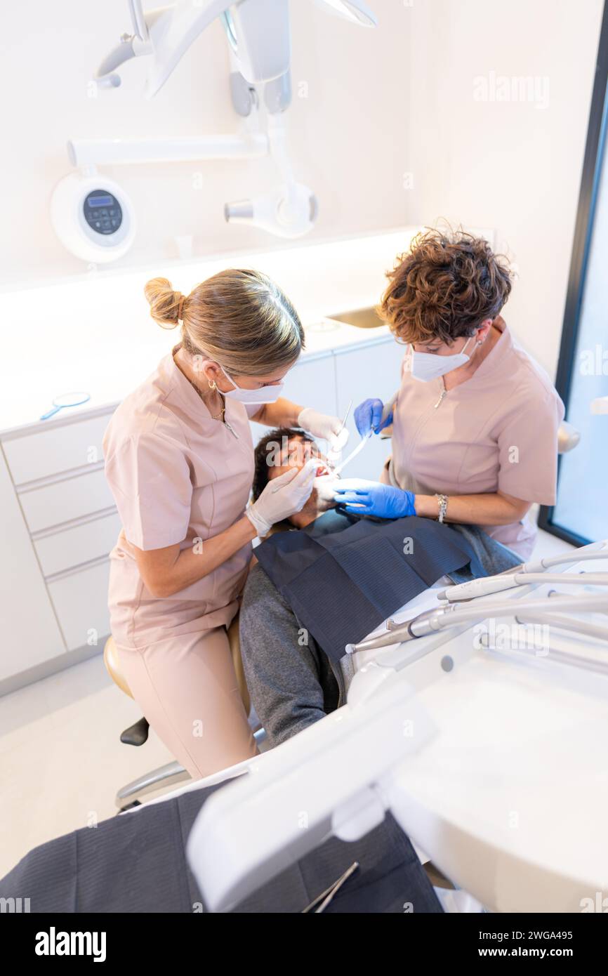 Dentist and assistant performing a mouth and teeth checkup on a young ...