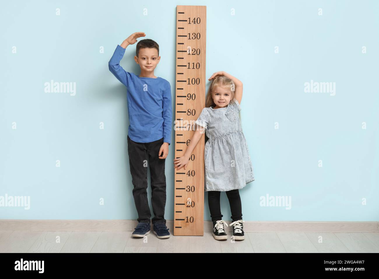 Cute little children measuring height near blue wall Stock Photo - Alamy