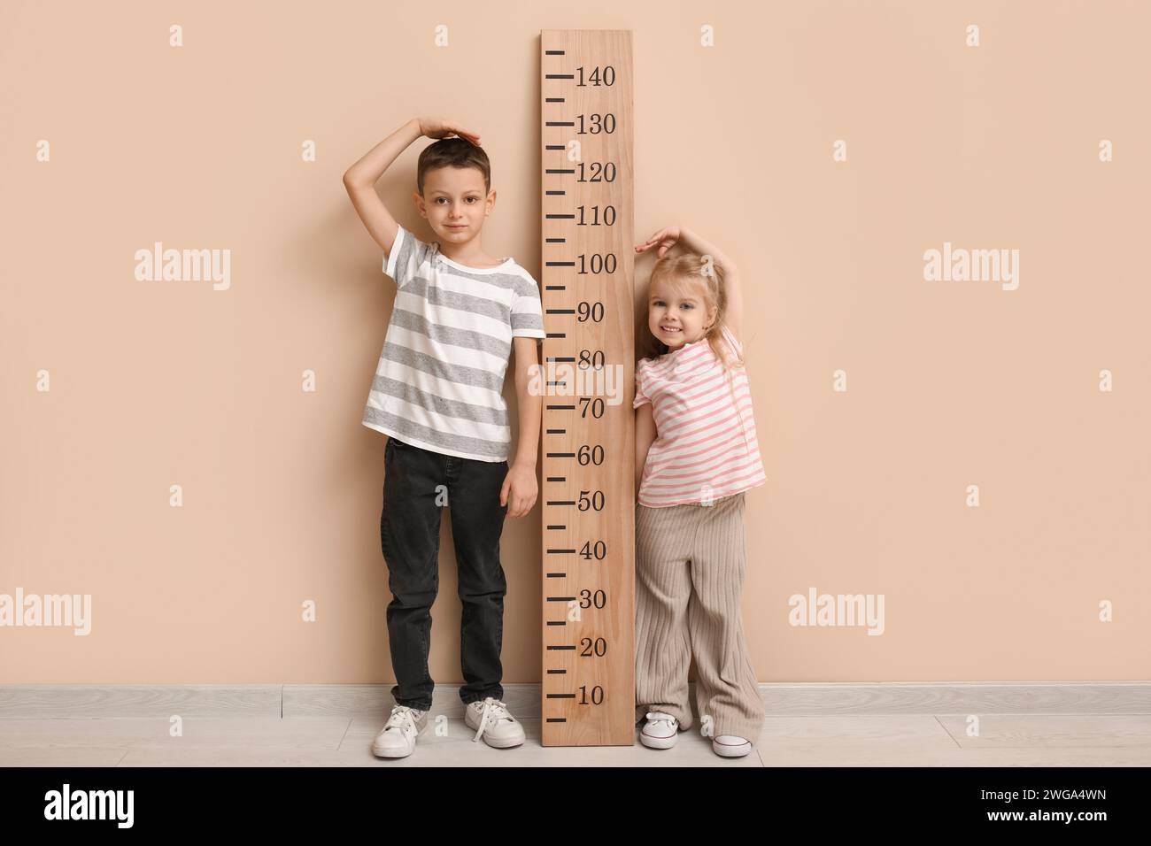 Cute little children measuring height near beige wall Stock Photo - Alamy