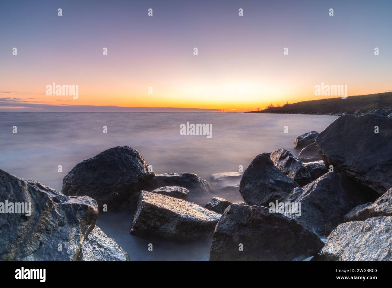 Sunrise between the rocks at the IJsselmeer. The low angle creates a ...
