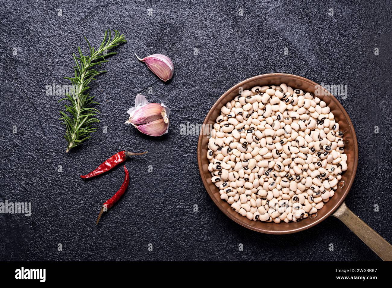Dried cowpeas in copper pan with garlic and rosemary on black textured ...