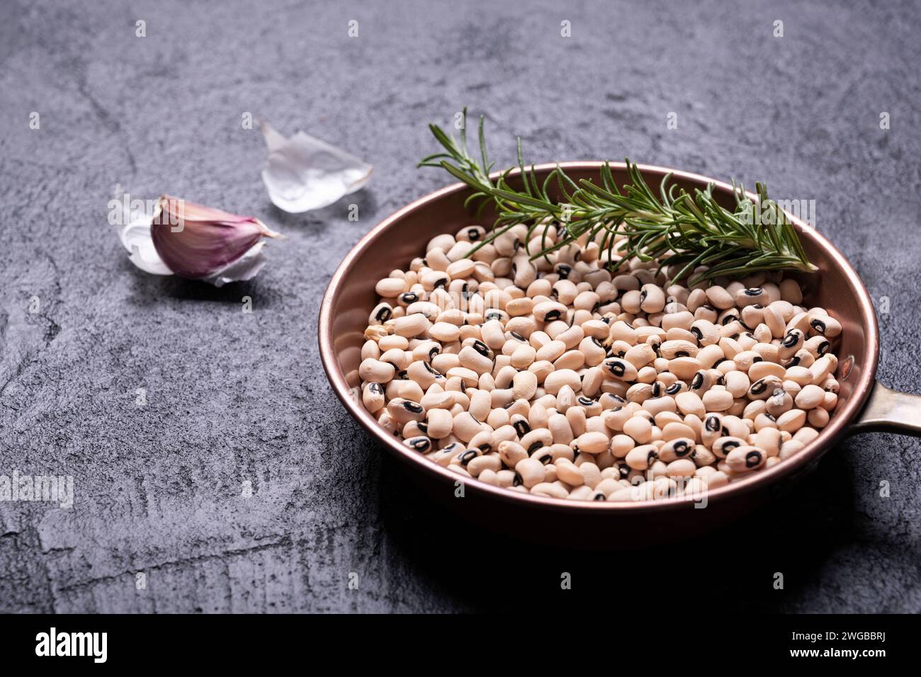 Dried cowpeas in copper pan with garlic and rosemary on black textured ...