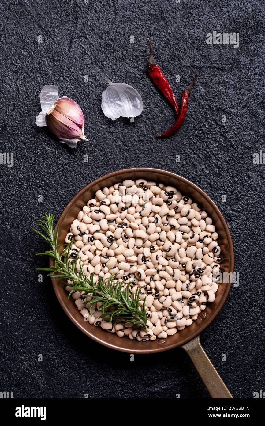 Dried cowpeas in copper pan with garlic and rosemary on black textured ...