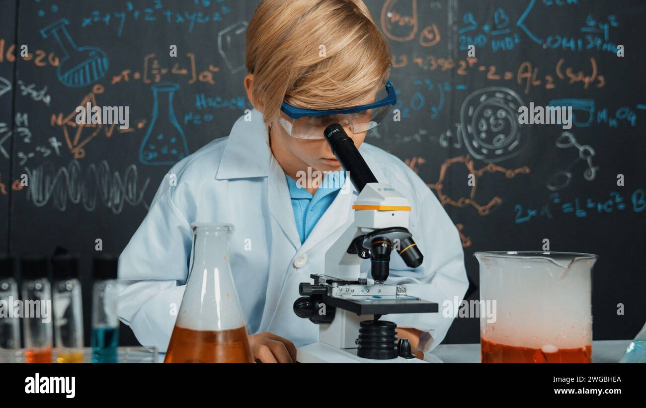 Smart boy using microscope analysis sample at science laboratory in STEM science class or ...