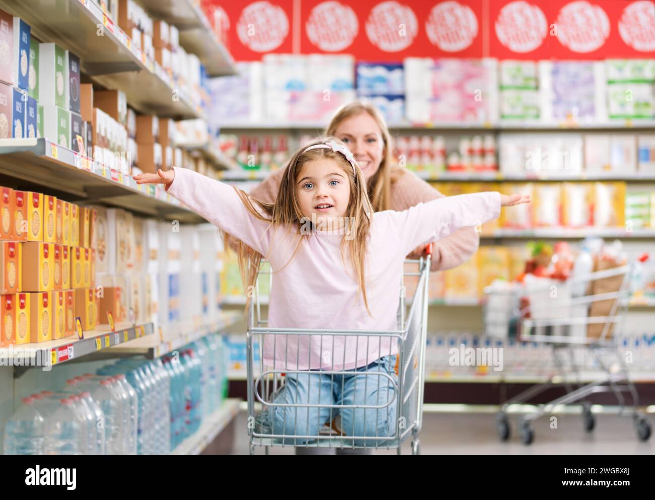 Cheerful cute girl sitting in a shopping cart at the supermarket, her ...