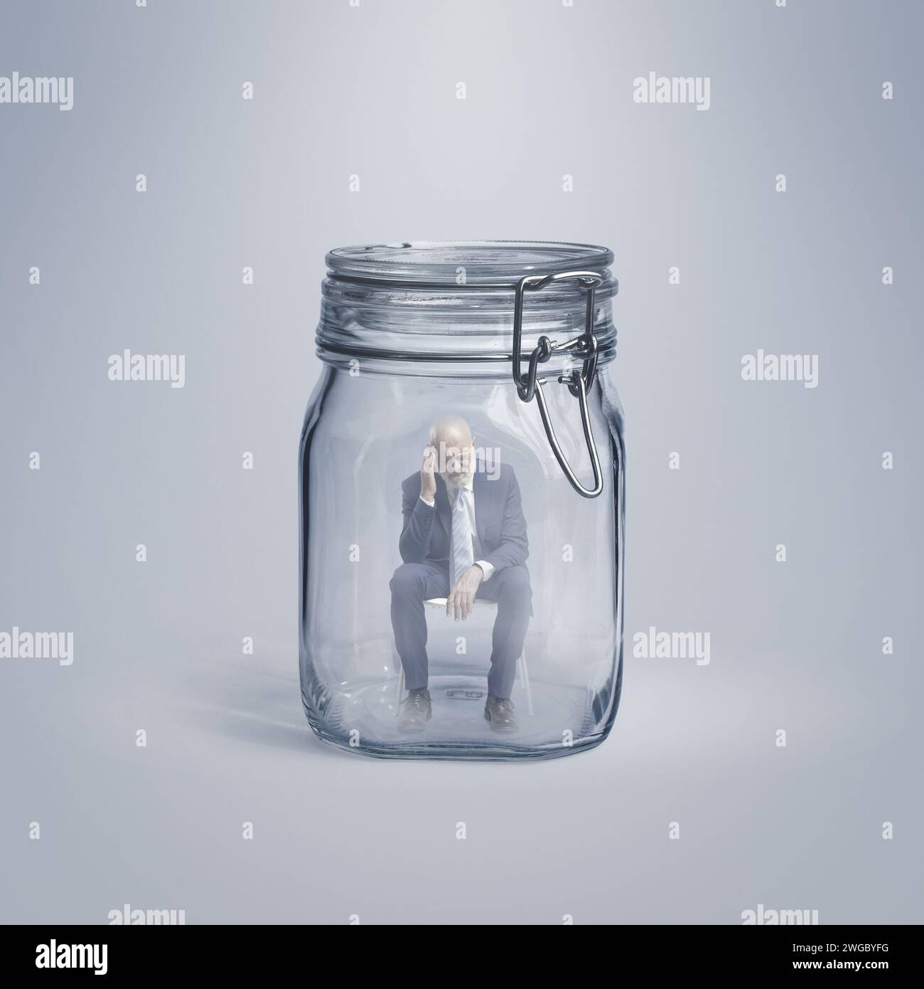 Hopeless senior businessman trapped inside a glass jar, he is sitting ...