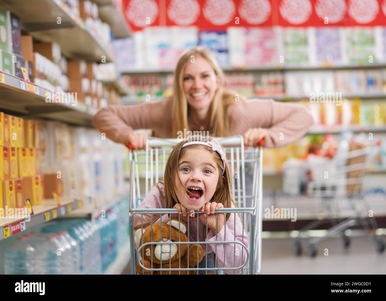 Cheerful cute girl sitting in a shopping cart at the supermarket, her ...