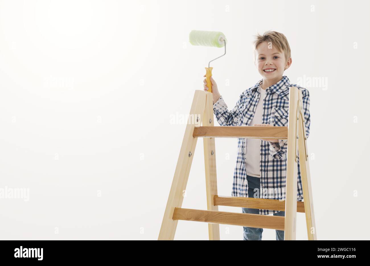 Cute smiling boy standing on a ladder and holding a paint roller, home ...