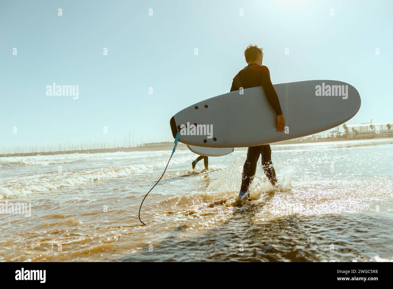 Back view of male surfer in wetsuit with his surfboard entering the sea ...