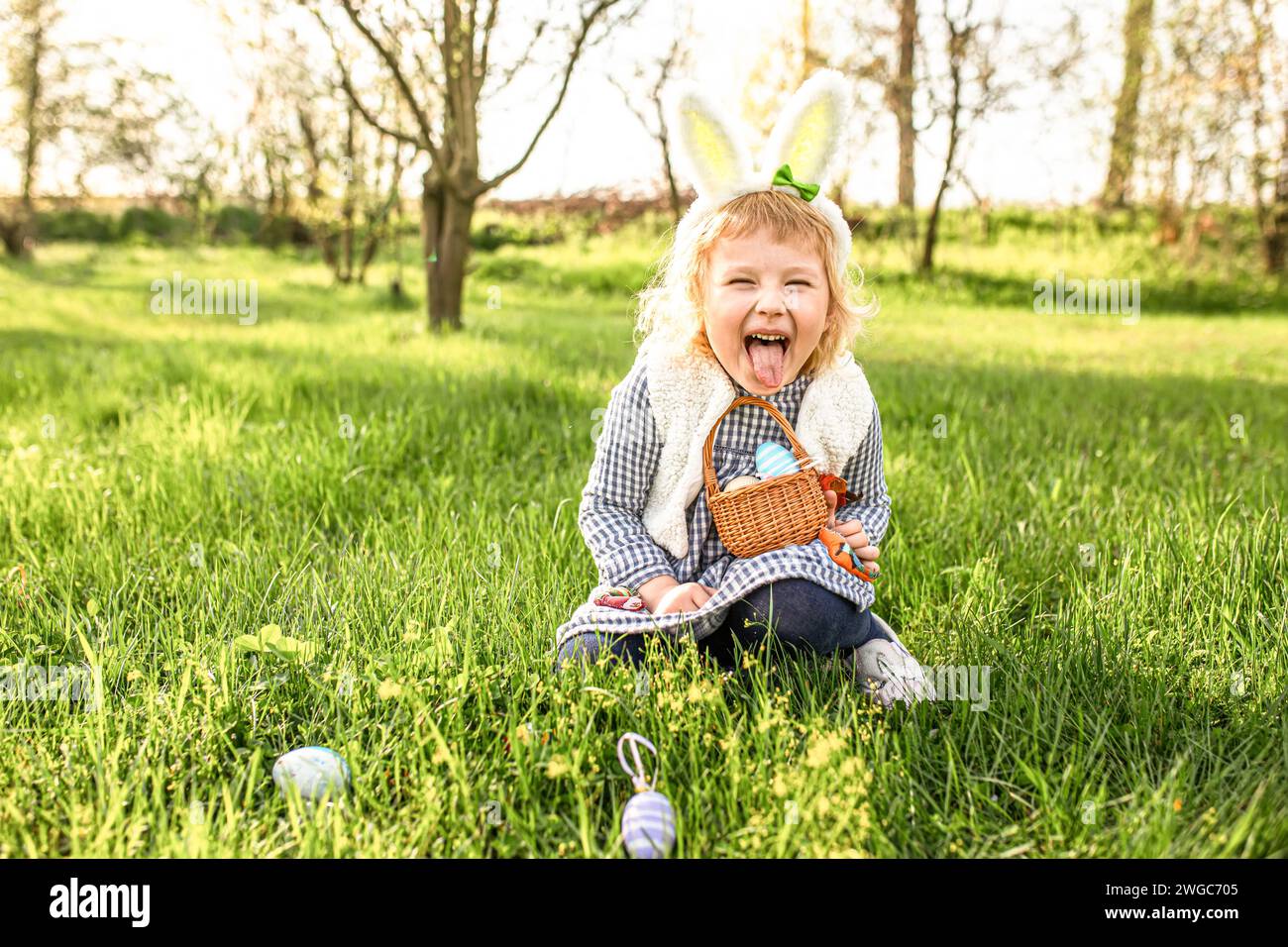 A girl wearing in the ears of an Easter bunny shows her tongue. A child ...