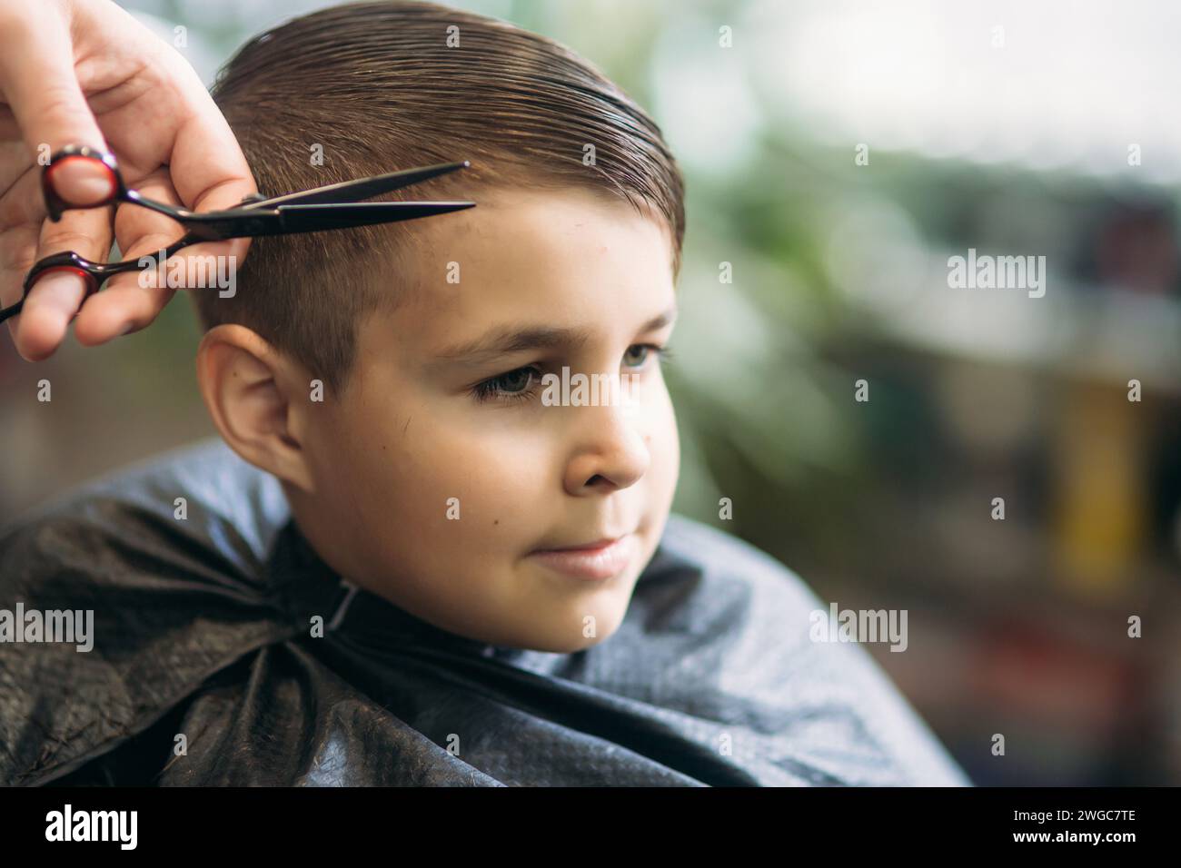 The boy getting haircut by scissor in barbershop. Barber use scissor ...