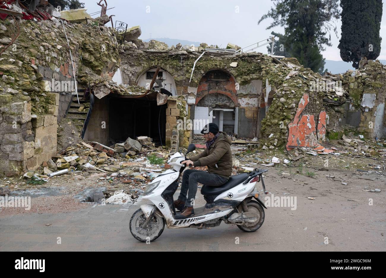 Antakya, Turkey. 04th Feb, 2024. A man rides his moped past a destroyed ...
