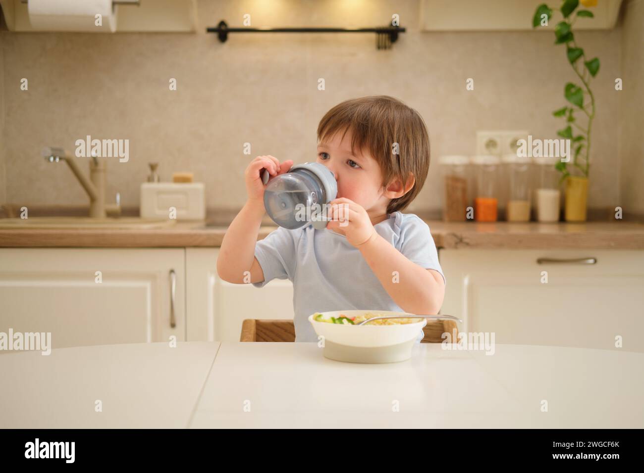 A child drinks from a non-watering cup while sitting at a table in a ...