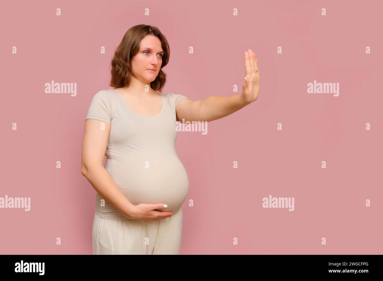 A pregnant woman shows a stop sign with her hand on a studio pink ...
