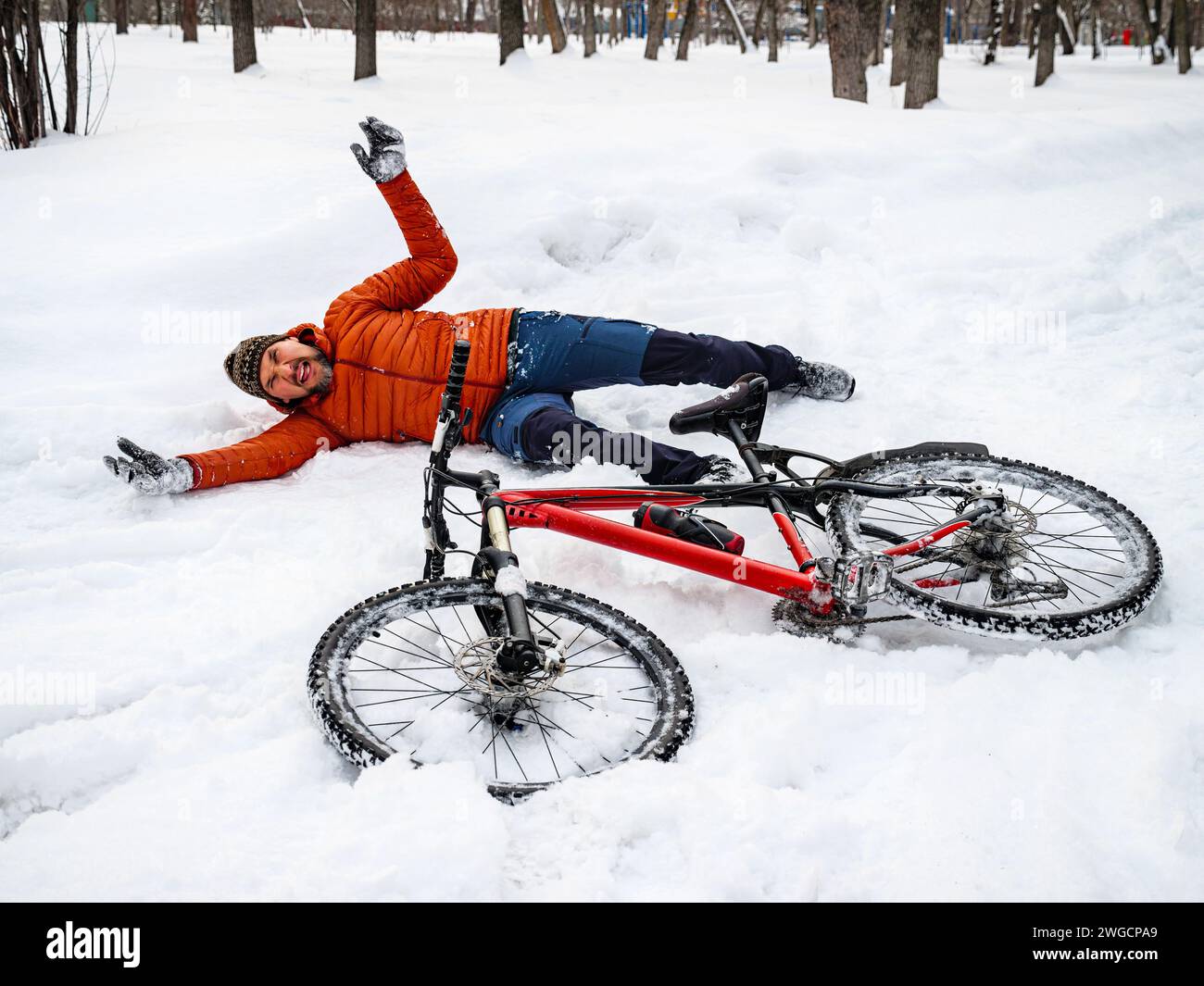 A guy fell off his bike in a winter park. A guy in an orange jacket ...