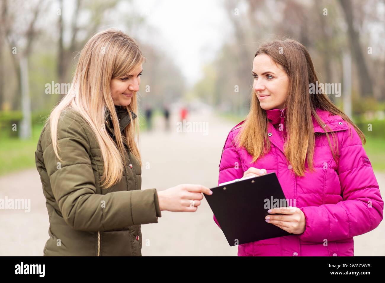 Two women engaged in a conversation with a clipboard on a park path ...