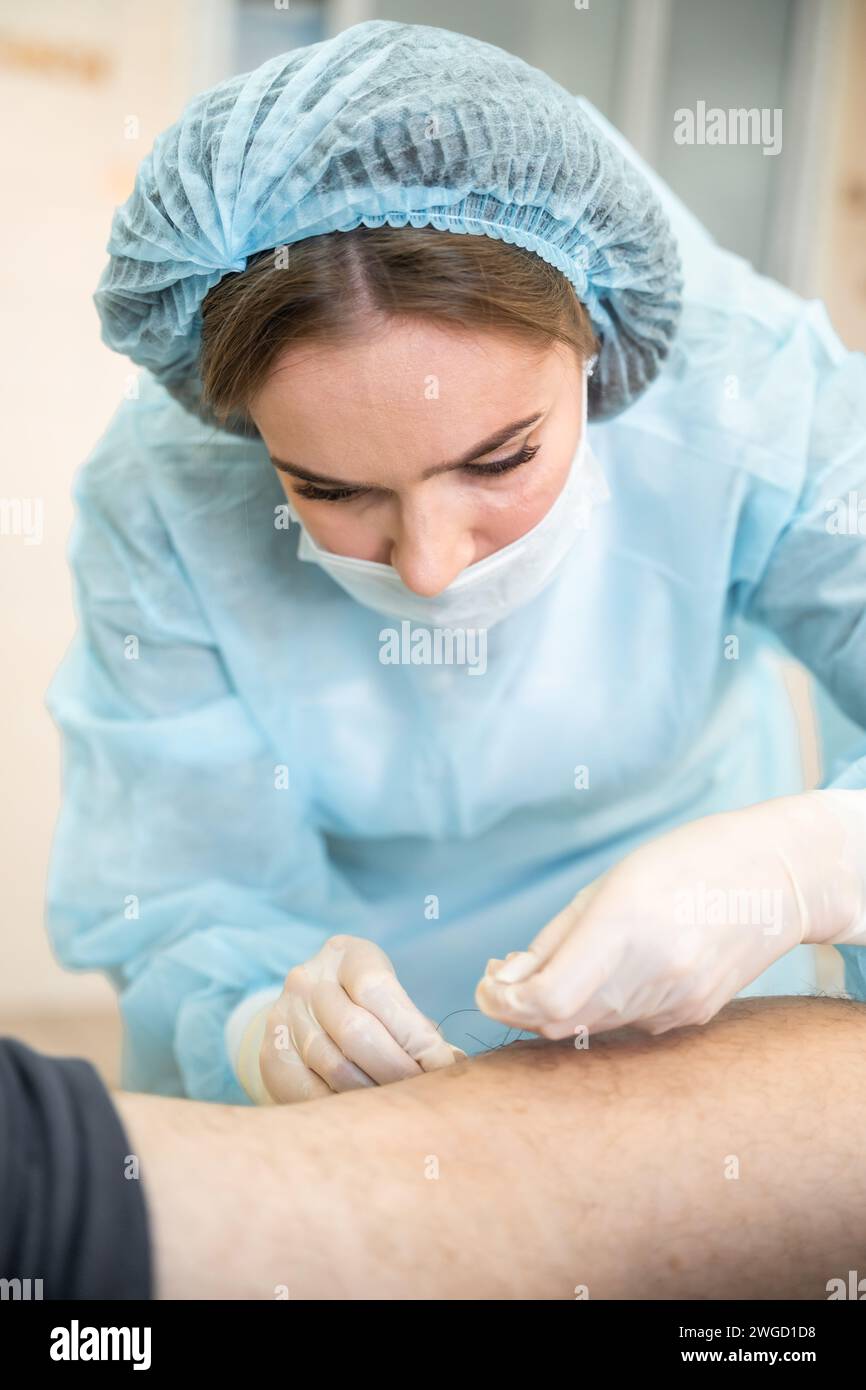 Portrait of dermatologist surgeon stitching up a wound after surgery ...