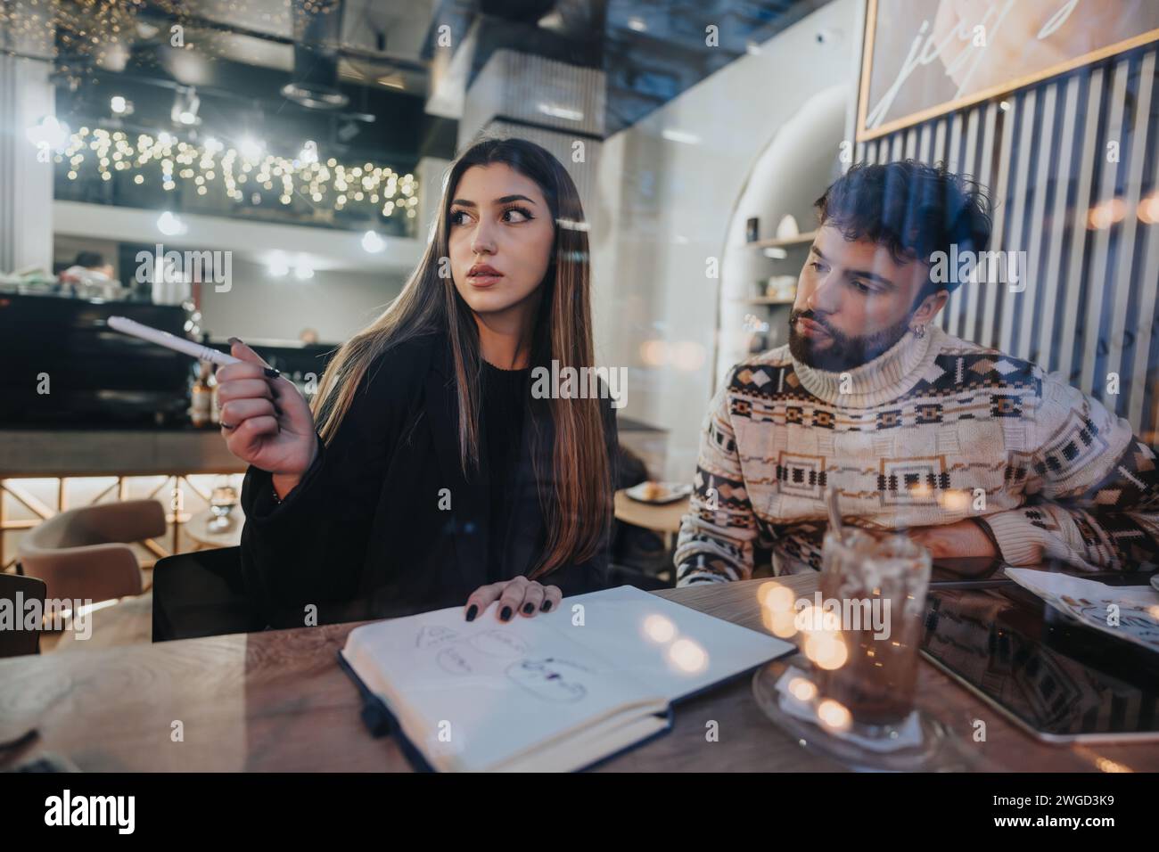 Two creative young people are engaged in a collaborative brainstorming session in a warmly lit ...