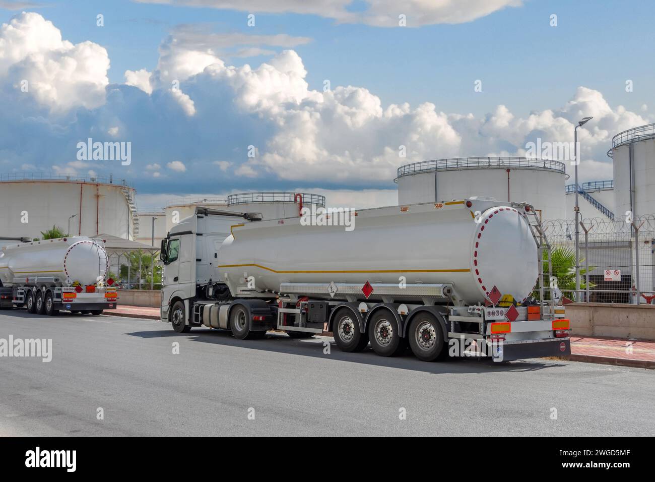 Trucks with trailers of white fuel tanks are parked next to a huge oil ...