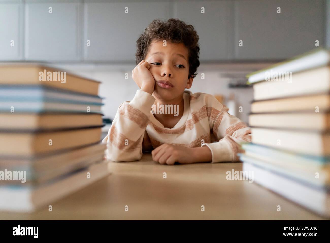 Bored black boy resting head on hand and looking at book stacks Stock ...
