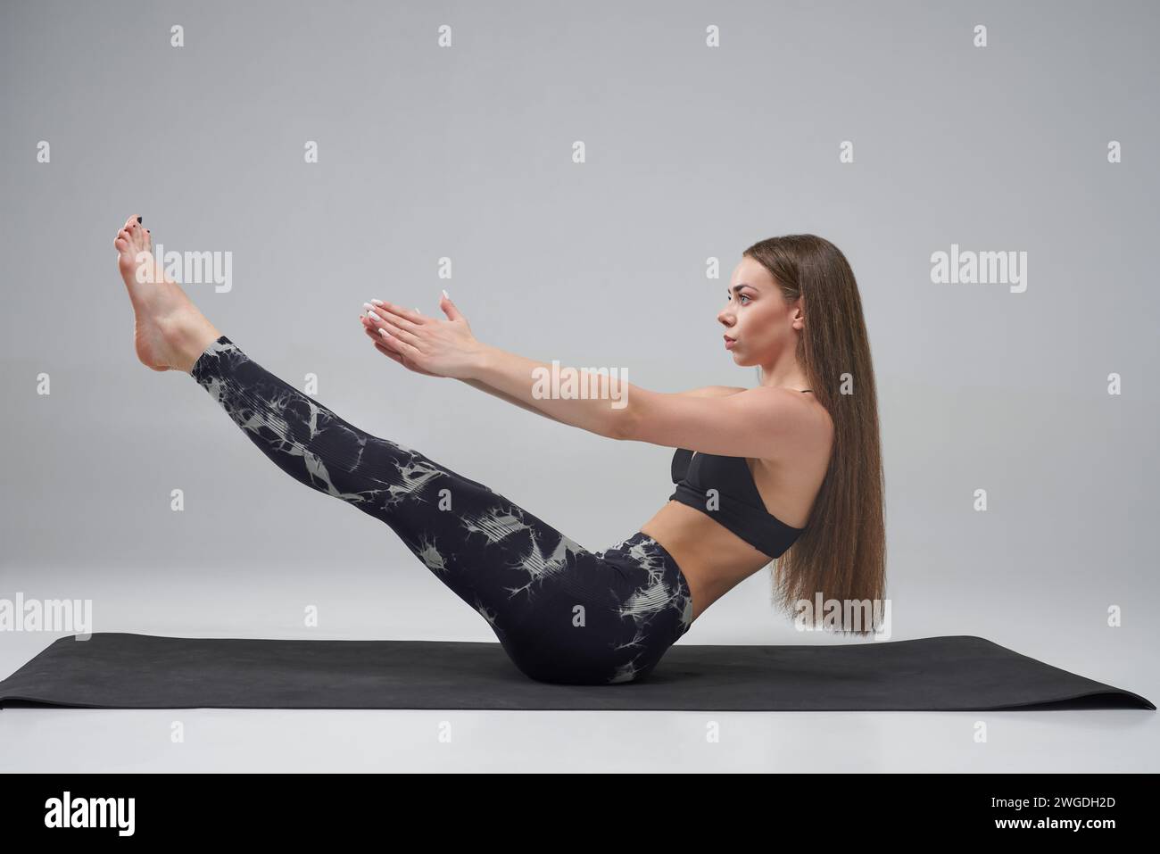 Mindful long-haired woman in dark legging doing boat pose of yoga. Side ...