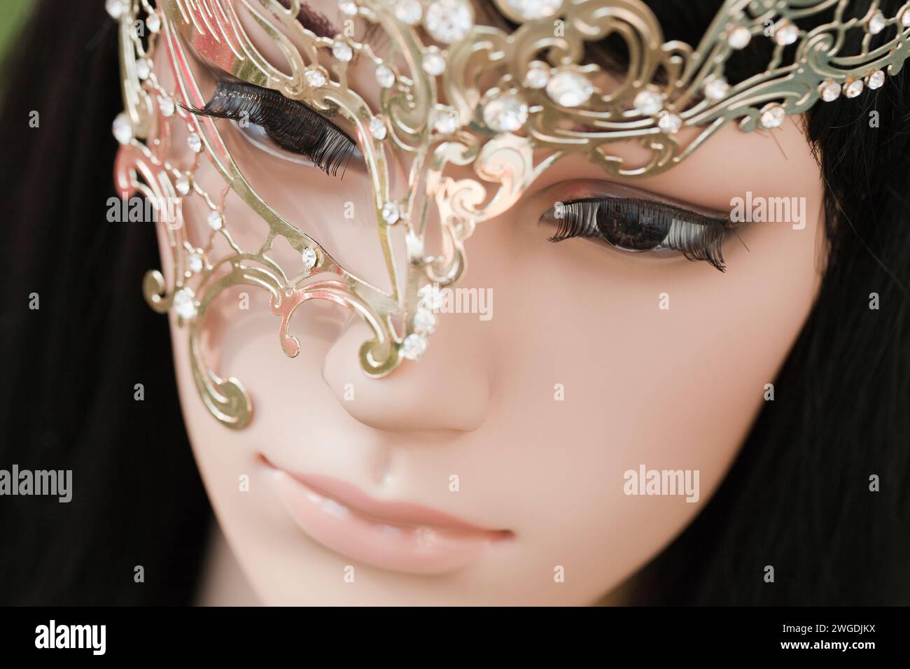 Plastic woman mannequin with black hair wearing a golden half mask with ...