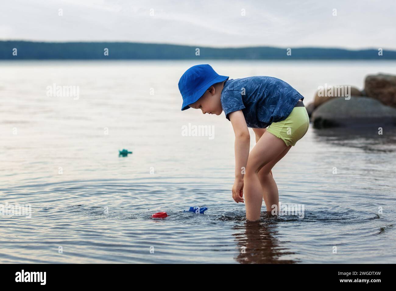 Kid boy playing with toy boat in sea water. Happy holiday by the sea ...