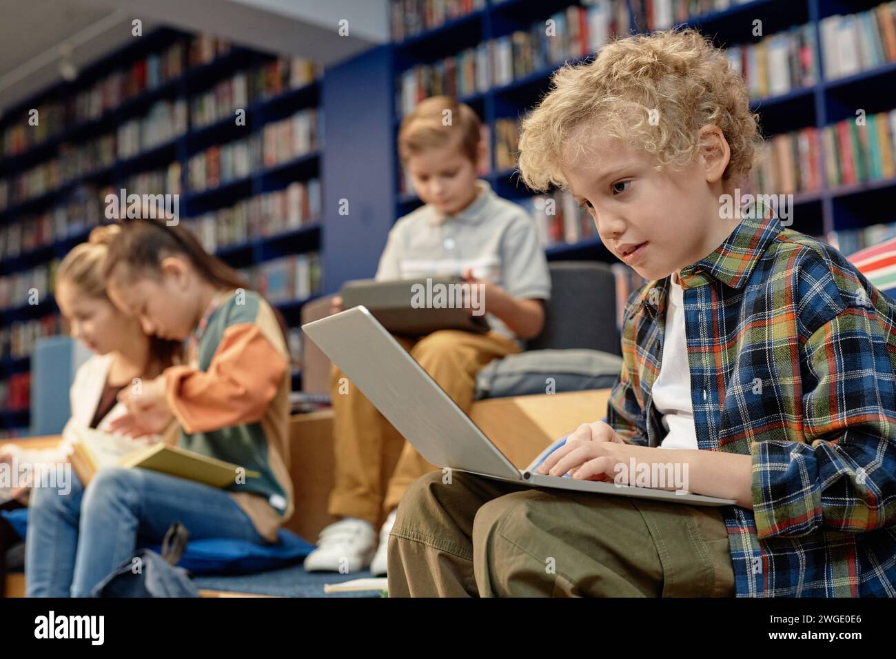 Side view portrait of blonde little boy using laptop in colorful school ...