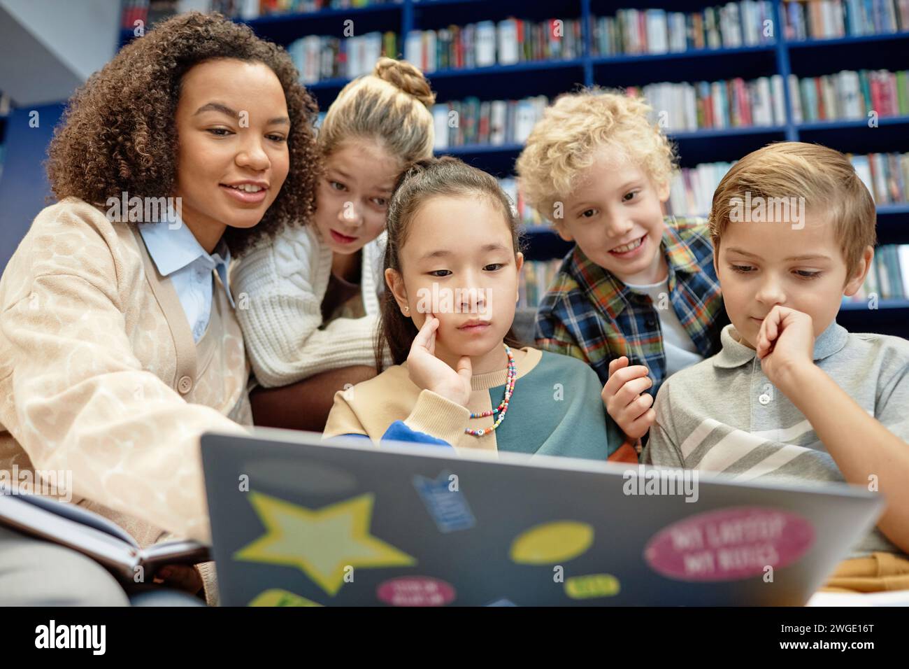 Front view at diverse group of children looking at laptop screen with ...