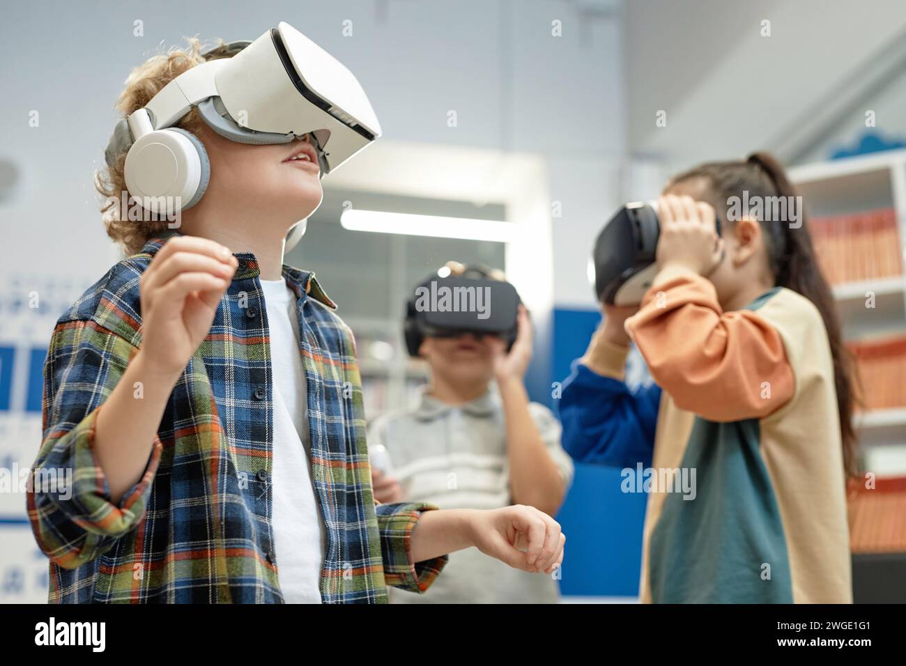 Portrait of excited blonde boy wearing VR headset in school library and ...