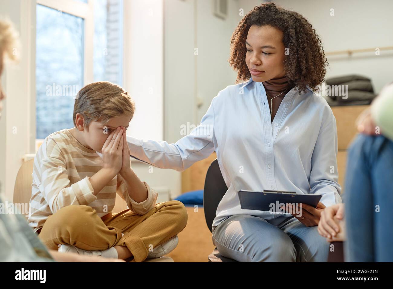 Portrait of young female therapist comforting troubled little boy in ...