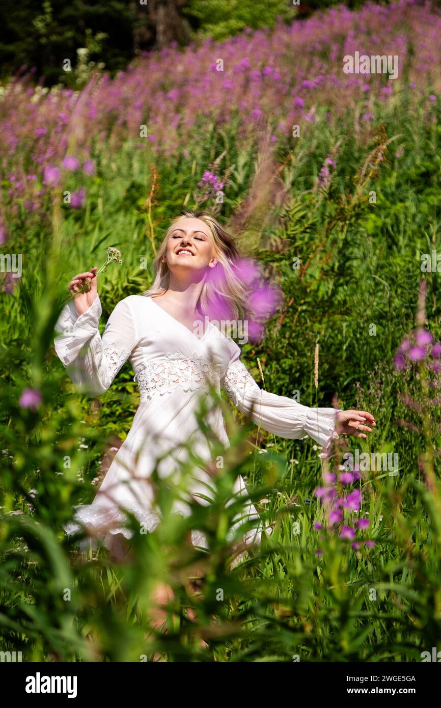 Young beautiful brunette woman walking through wildflowers in alpine meadow, summer dress ...