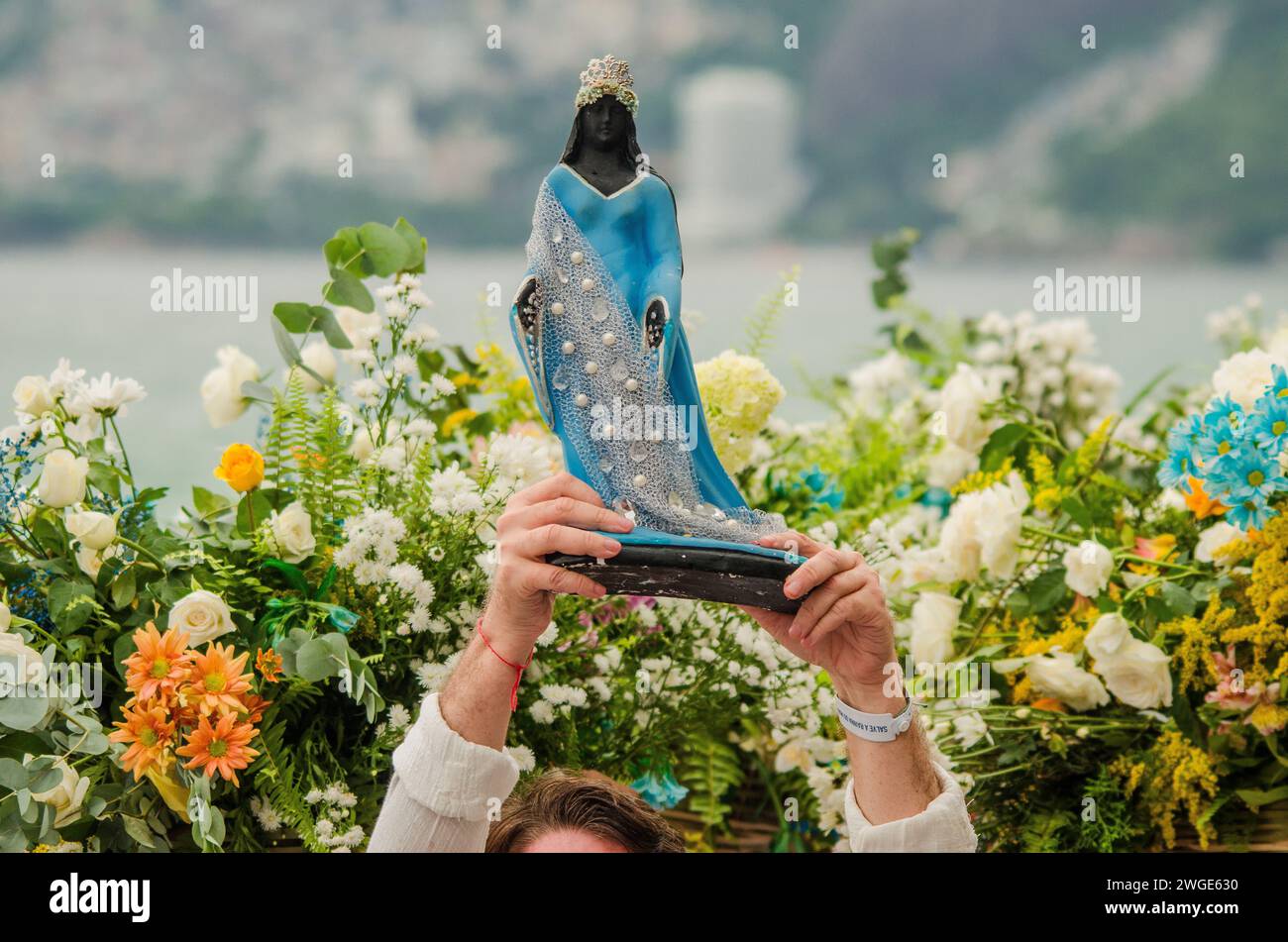 A devotee holds the statue of Iemanjá with flowers behind on Iemanjá's ...