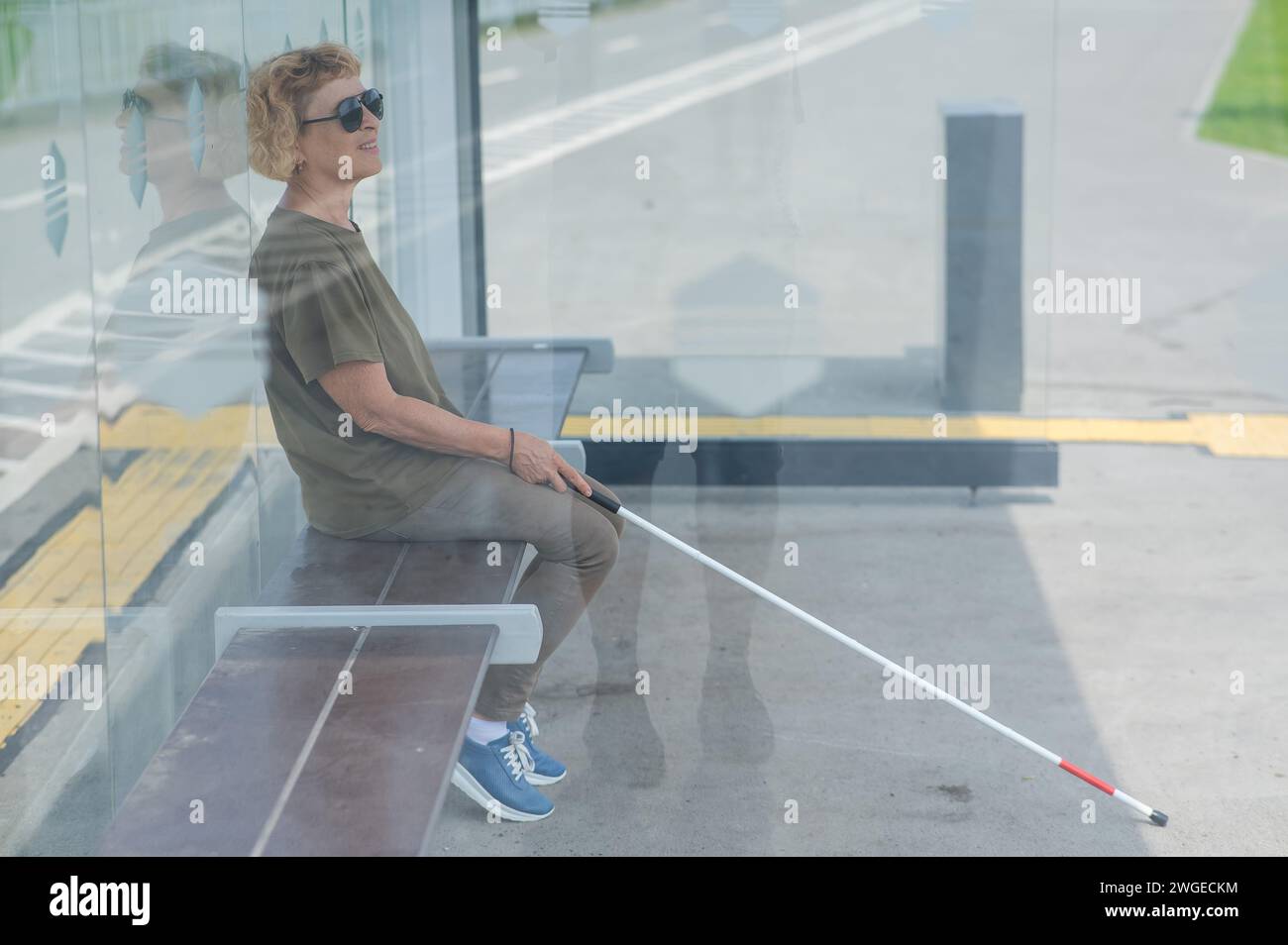 An elderly blind woman is waiting for transport at a bus stop Stock ...