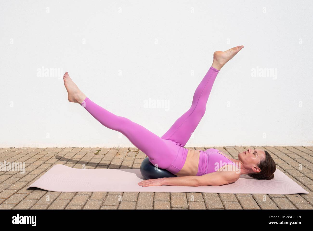fit sporty woman doing pilates ball exercises outside. scissor stretch ...